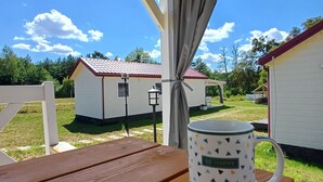 Uma mesa de madeira com uma caneca e um folheto, um alpendre coberto e vista para casas móveis.