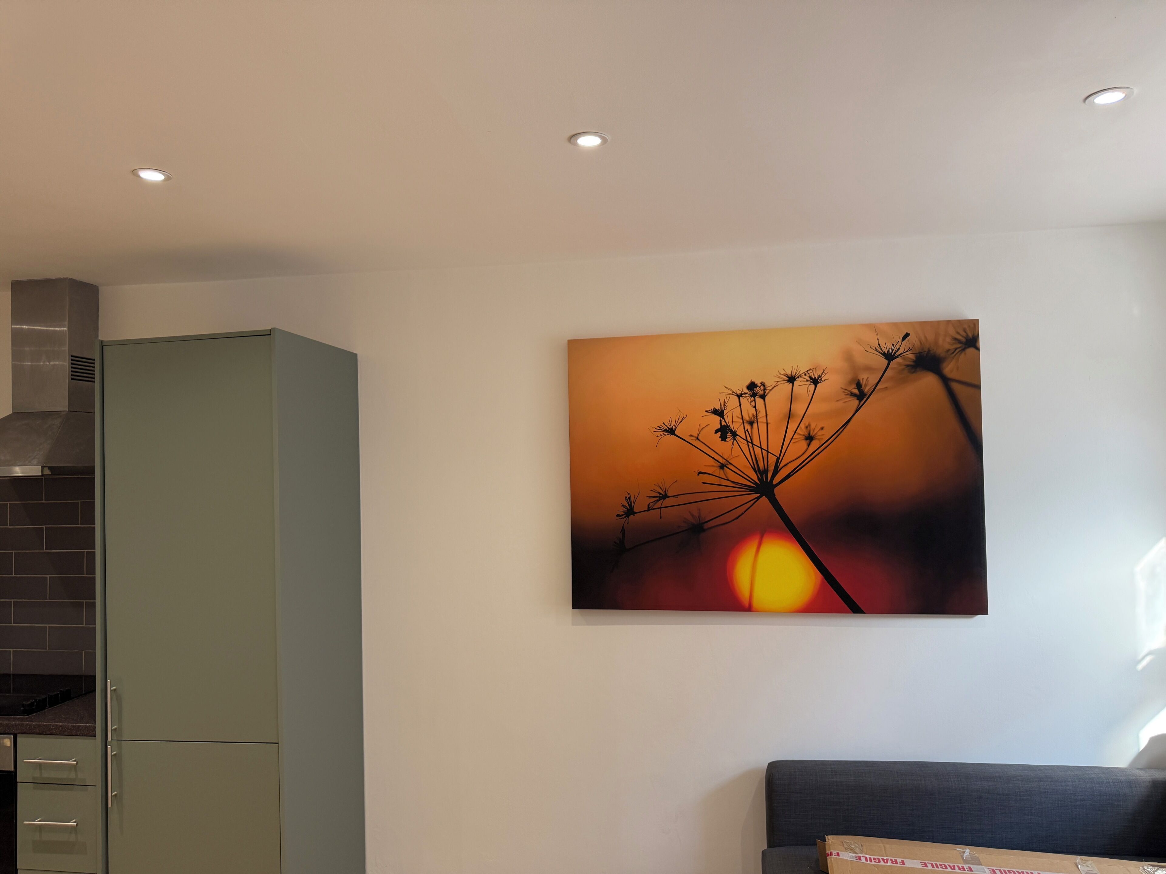Uma cozinha com design moderno, um armário cinza grande e um quadro pendurado na parede com um dente-de-leão ao pôr do sol.
