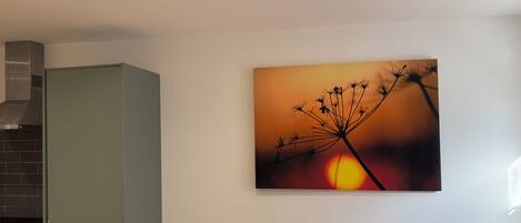 Uma cozinha com design moderno, um armário cinza grande e um quadro pendurado na parede com um dente-de-leão ao pôr do sol.
