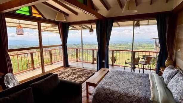 Quarto com cama, sofá, uma mesinha e vista para o exterior.