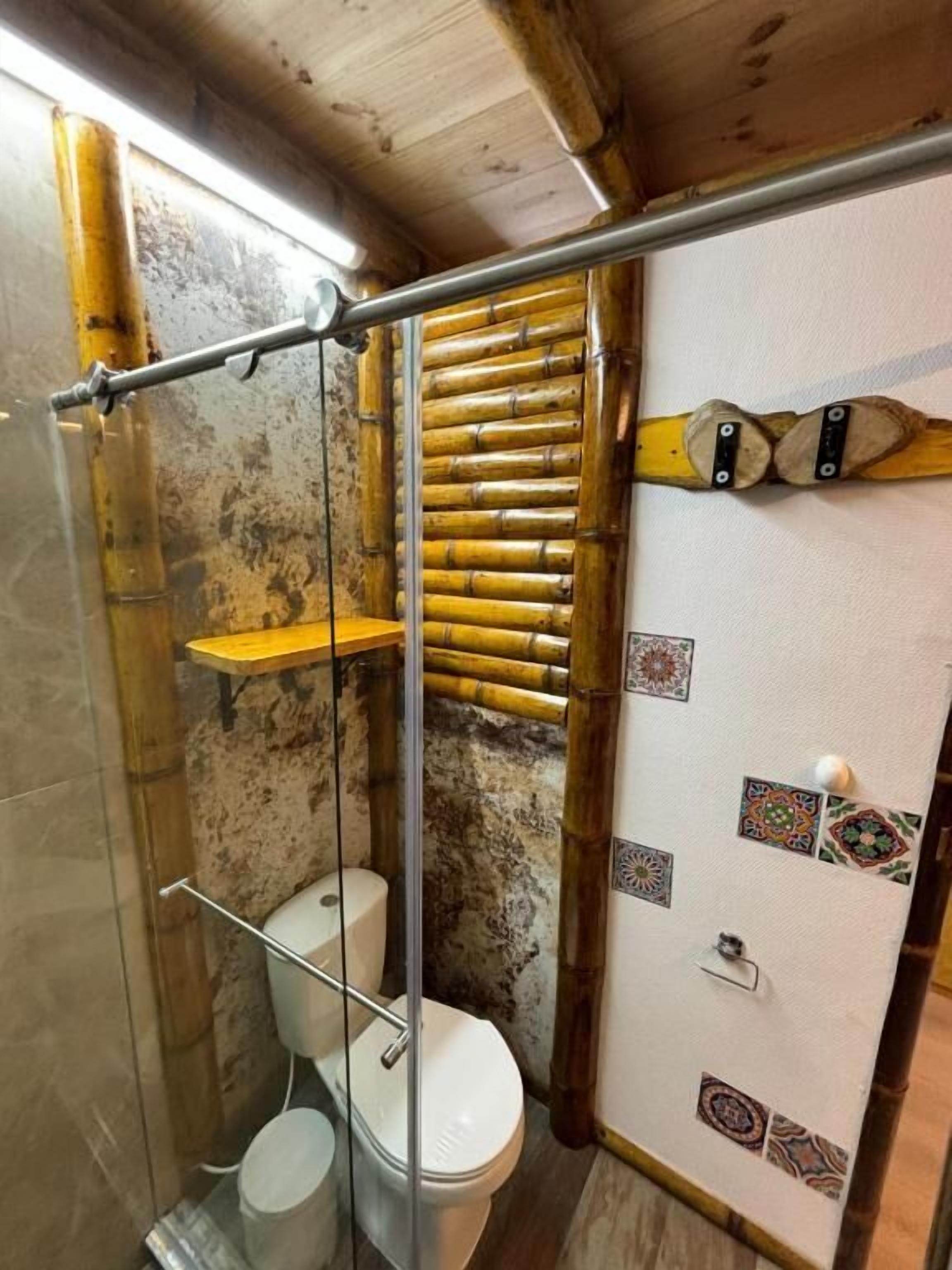 Uma casa de banho com cabine de duche em vidro, sanita e parede de madeira com azulejos decorativos.