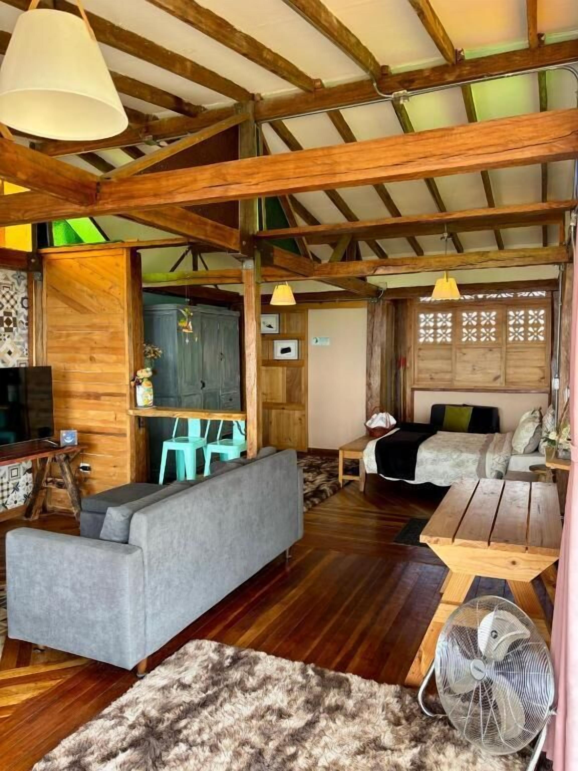 Um interior rústico com vigas de madeira, um sofá, uma mesa e um ventilador.