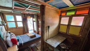 Um quarto rústico com uma cama, uma pequena mesa de madeira e uma janela com vidros coloridos.