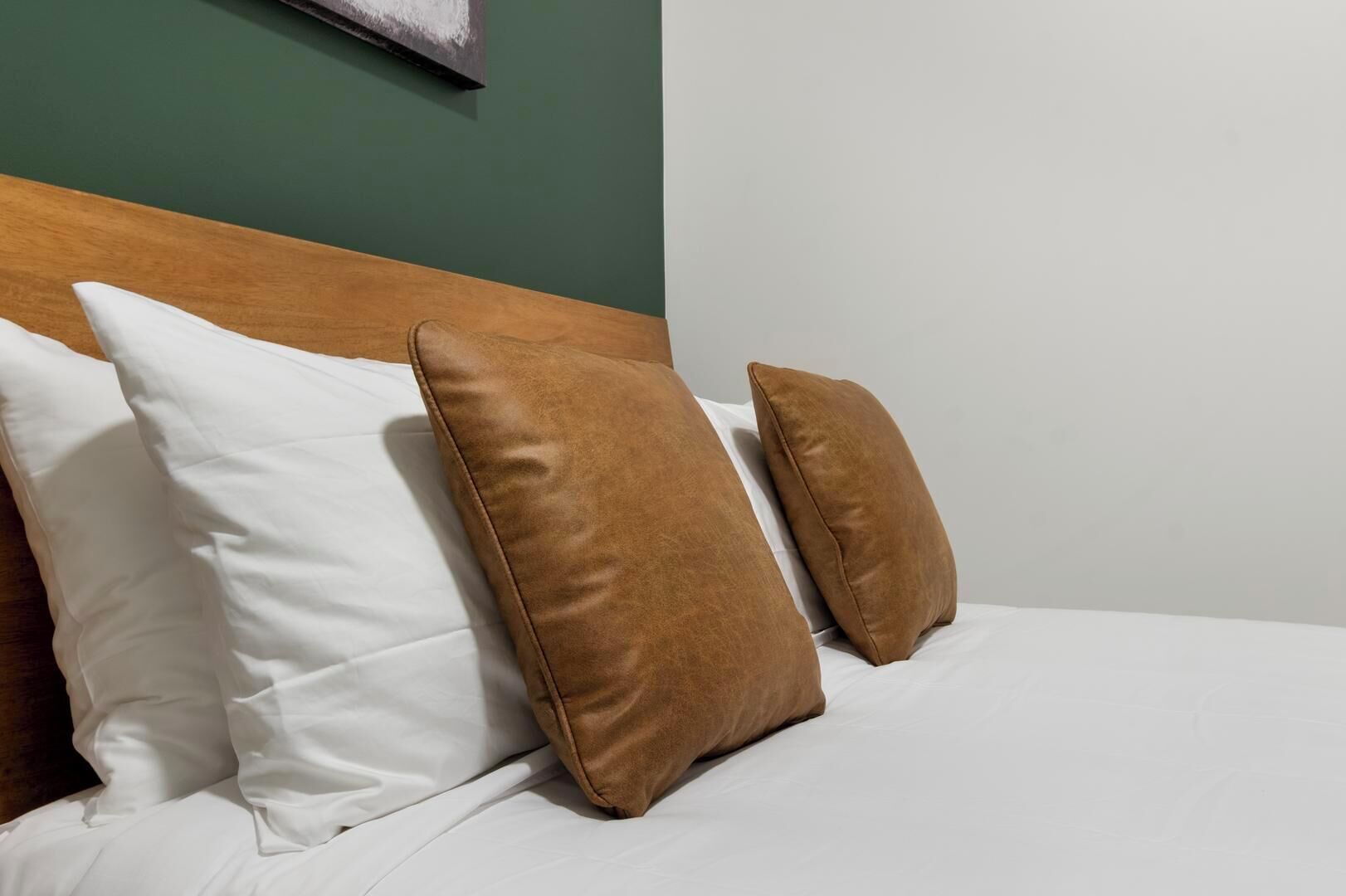 Uma cama com almofadas brancas e castanhas, cabeceira de madeira e parede verde.