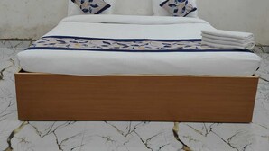 Cama com base de madeira, roupa de cama branca e almofadas estampadas.