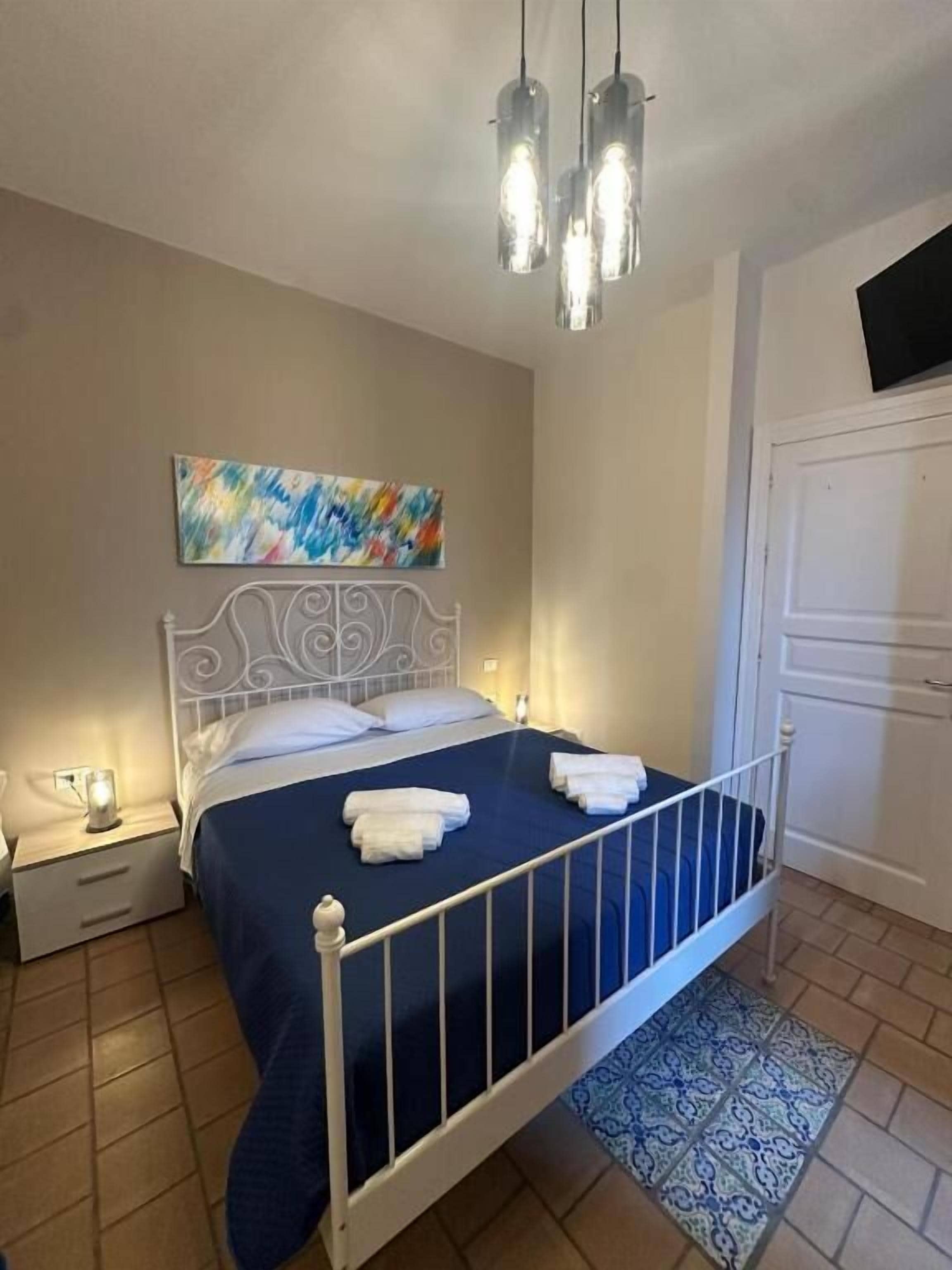 Quarto com cama, mesas de cabeceira, um quadro, guarda-roupa e tapete estampado.