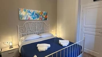 Quarto com cama, mesas de cabeceira, um quadro, guarda-roupa e tapete estampado.