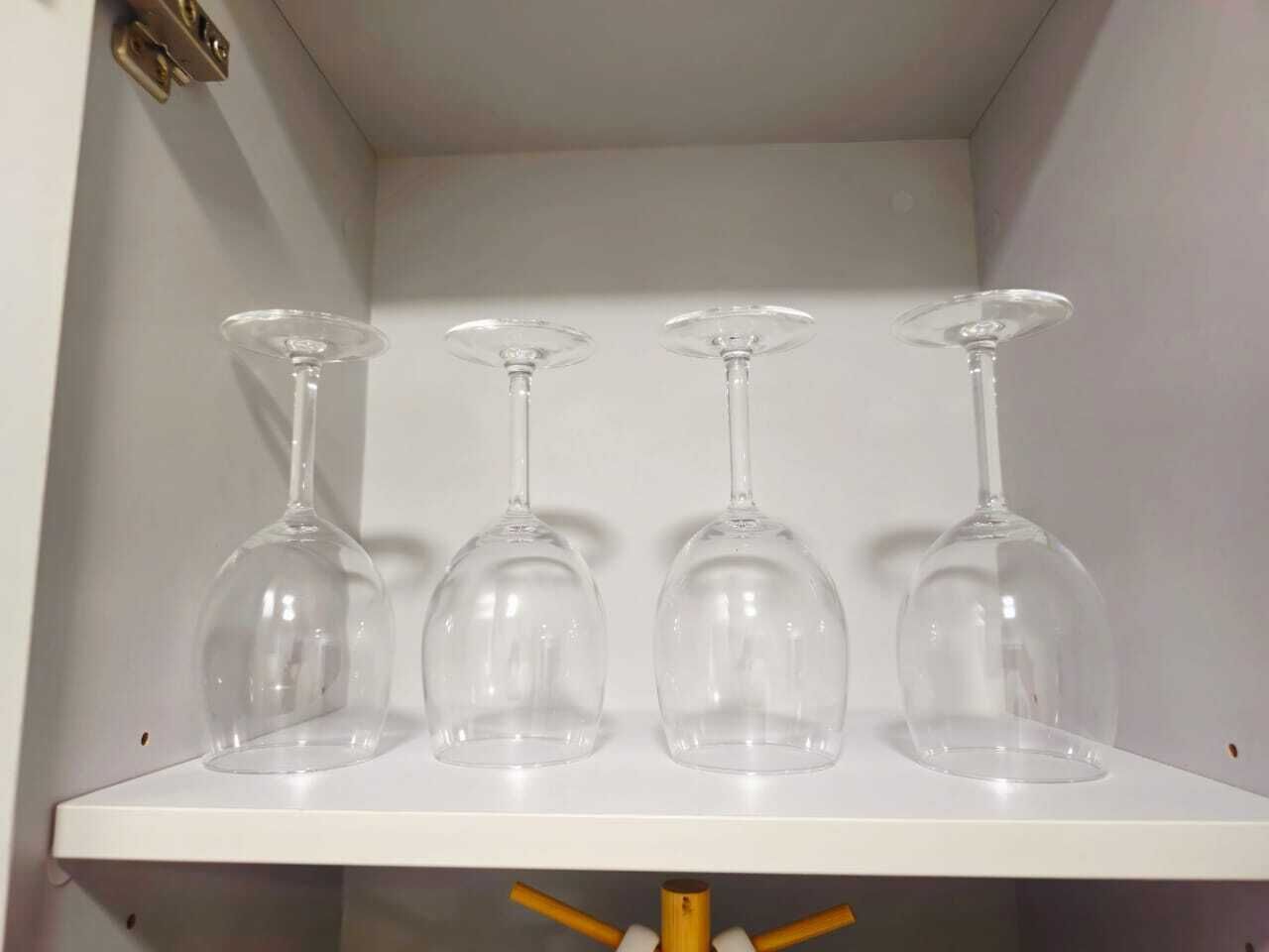Uma estante branca com quatro copos de vinho transparentes.