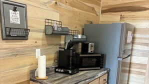 Uma cozinha compacta com armários de madeira, uma lixeira de aço inoxidável, cafeteira, micro-ondas e geladeira.