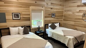 Quarto com duas camas, paredes de madeira, uma janela, uma mesinha de cabeceira e quadros emoldurados.