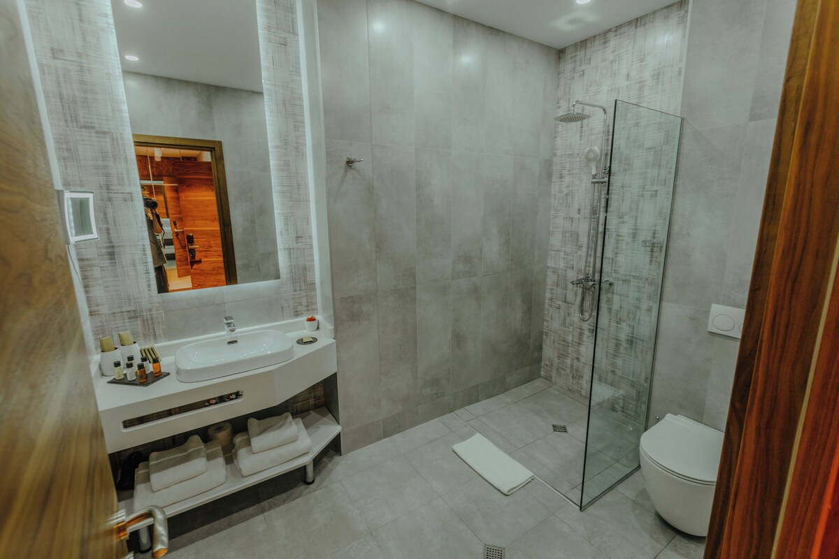 Casa de banho moderna com cabine de chuveiro de vidro, lavatório branco com espelho e sanita.
