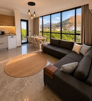 Uma sala de estar moderna com um sofá grande, área de jantar, cozinha e janelas amplas com vista para uma paisagem montanhosa.