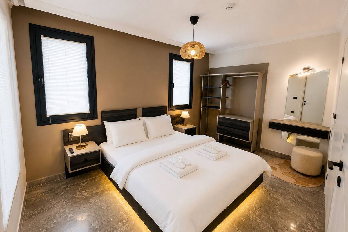 Quarto de hotel com uma cama grande, luminárias de cabeceira, um guarda-roupa, um espelho e uma pequena mesa redonda.