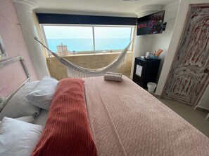 Quarto de hotel com cama, almofadas, rede, vista para o mar, sinal da Netflix e porta com padrão decorativo.
