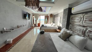 Quarto de hotel moderno com uma cama grande, um sofá, uma TV e vista para o mar.
