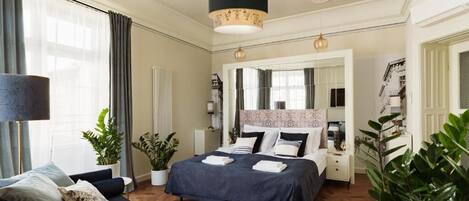 Quarto moderno com uma cama grande, mesas de cabeceira, um criado-mudo, uma planta em vaso e um lustre.