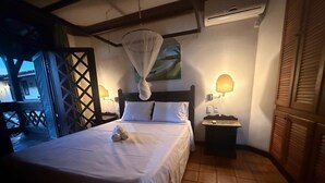 Uma cama com dossel, uma mesinha de cabeceira com abajur e vista para uma varanda.