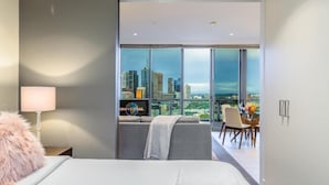 Quarto de hotel moderno com uma cama grande, um sofá, um espaço de refeições e vista para a cidade.
