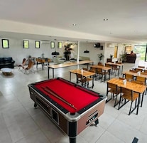 Mesa de bilhar, mesas de jantar, cadeiras e um bar numa área ampla e coberta.