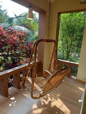Uma cadeira de balanço de vime sobre um deck de madeira, com vista para um verde exuberante.