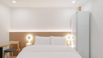 Quarto de hotel com cama, abajures, escrivaninha e uma cadeira.