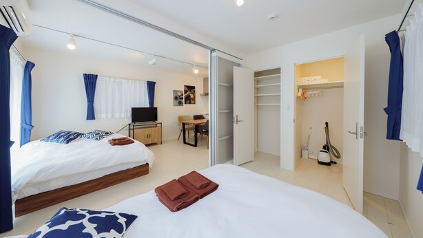Quarto de hotel com duas camas, uma escrivaninha, uma cadeira, uma televisão, um armário e um aspirador de pó.