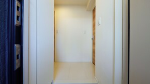 Um corredor estreito com uma porta no final, um interruptor de luz na parede e uma maçaneta à esquerda.