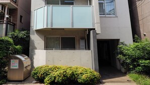 Um edifício residencial com vários andares, varandas, uma abertura para correspondência e um pequeno jardim.