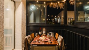 Uma área de refeições com mesa de madeira, cadeiras, uma garrafa de vinho, tábua de queijos e um fogão a gás.