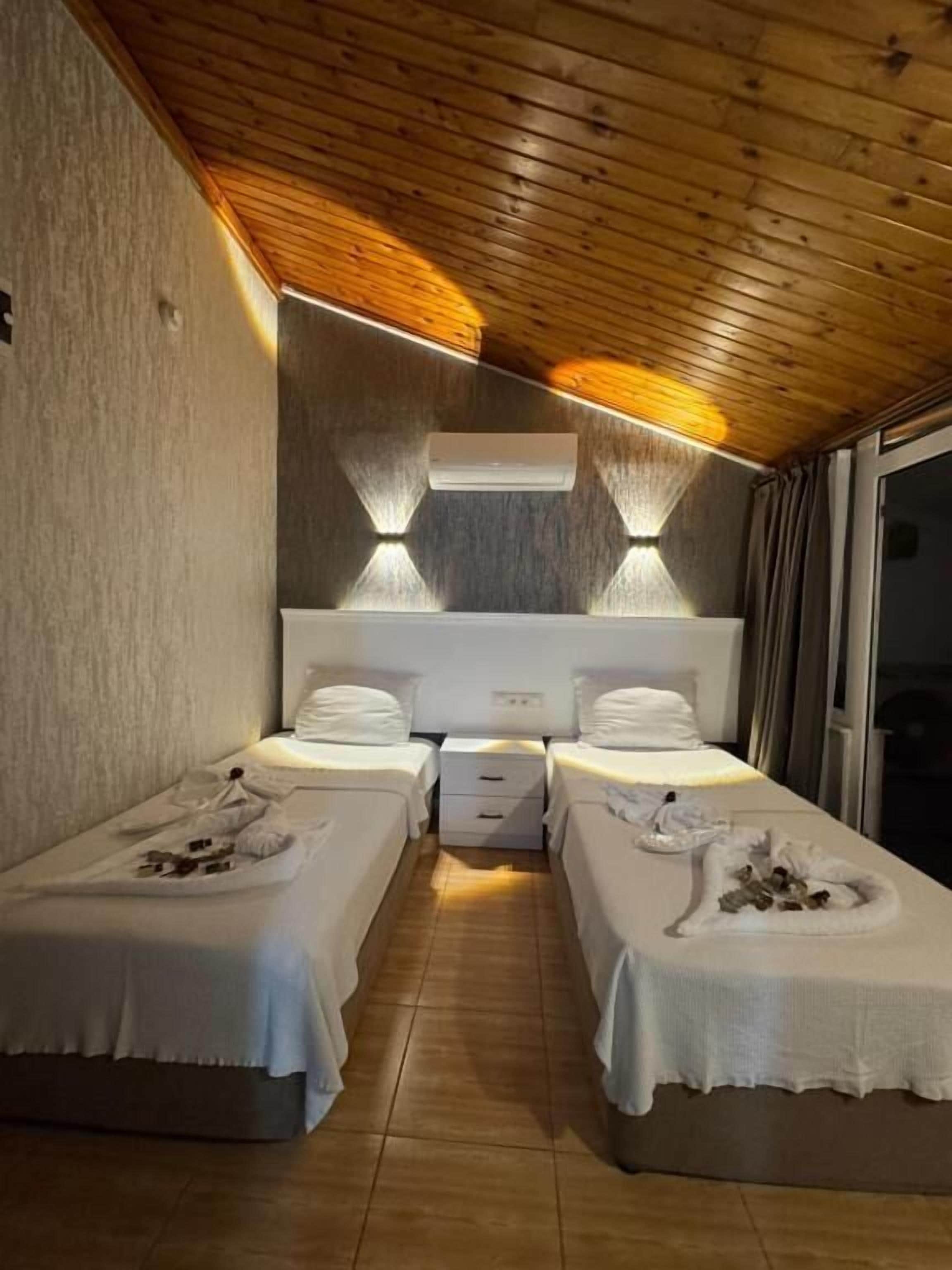Quarto de hotel com duas camas de solteiro, teto de madeira e uma pequena janela.