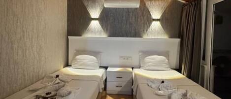 Quarto de hotel com duas camas de solteiro, teto de madeira e uma pequena janela.