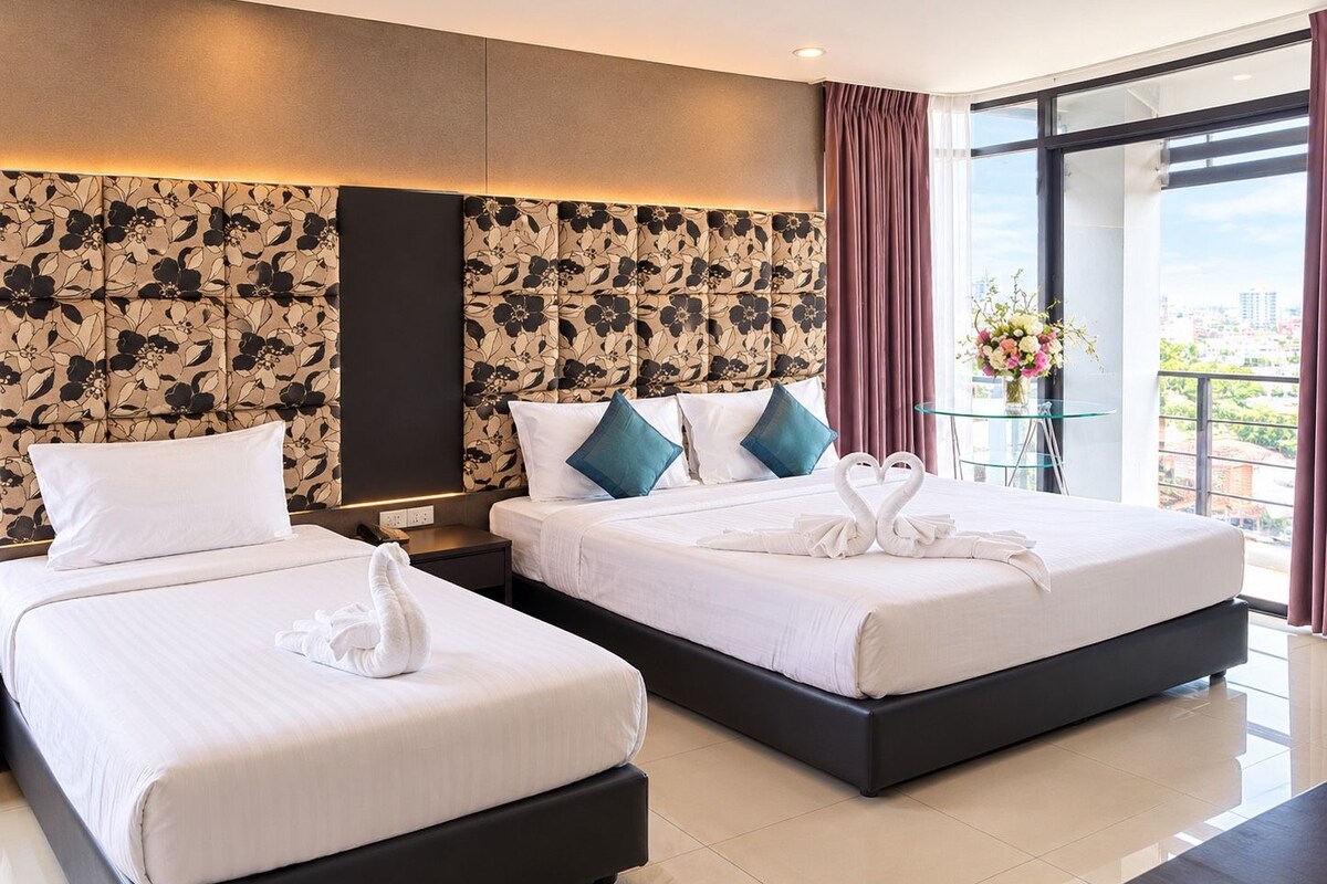 Quarto de hotel com duas camas, uma janela grande e vista para a cidade.