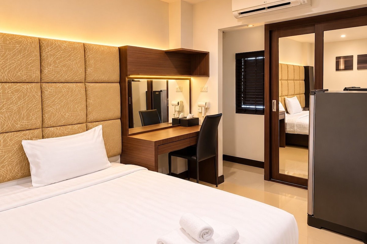 Quarto de hotel com cama, escrivaninha, cadeira, espelho, armário e ar condicionado.