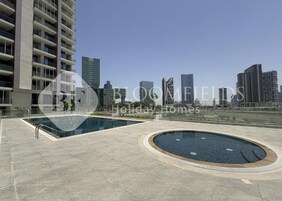 Um edifício residencial moderno com área de piscina no terraço, apresentando uma piscina retangular grande e uma banheira de hidromassagem circular, com o horizonte da cidade ao fundo.