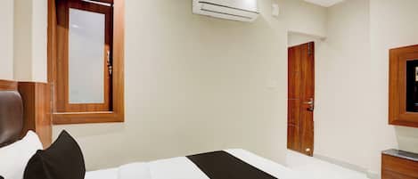 Quarto de hotel com cama, guarda-roupa de madeira, espelho e unidade de ar condicionado.