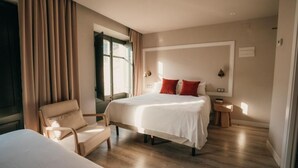 Quarto de hotel com cama, cadeira, mesa de cabeceira e janela.