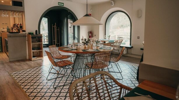 Uma área de refeições com uma mesa redonda, cadeiras de vime e um chão estampado.