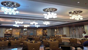 Um saguão de hotel com várias áreas de estar, lustres e um balcão de recepção.
