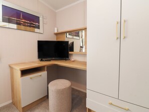 Quarto com escrivaninha, televisão, armário e um banquinho pequeno.