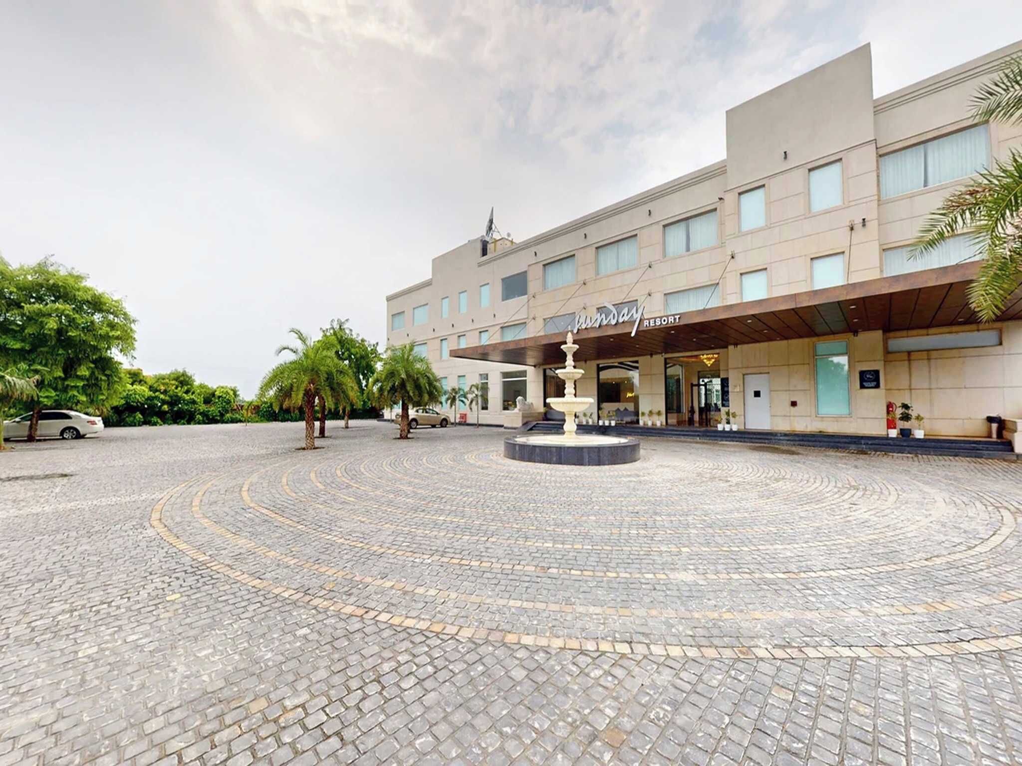 Um hotel com um pátio pavimentado, uma fonte e fachada de edifício moderna.