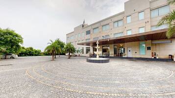 Um hotel com um pátio pavimentado, uma fonte e fachada de edifício moderna.