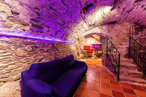 Um interior de paredes de pedra com um sofá roxo, uma escada e um letreiro de bicicleta neon.