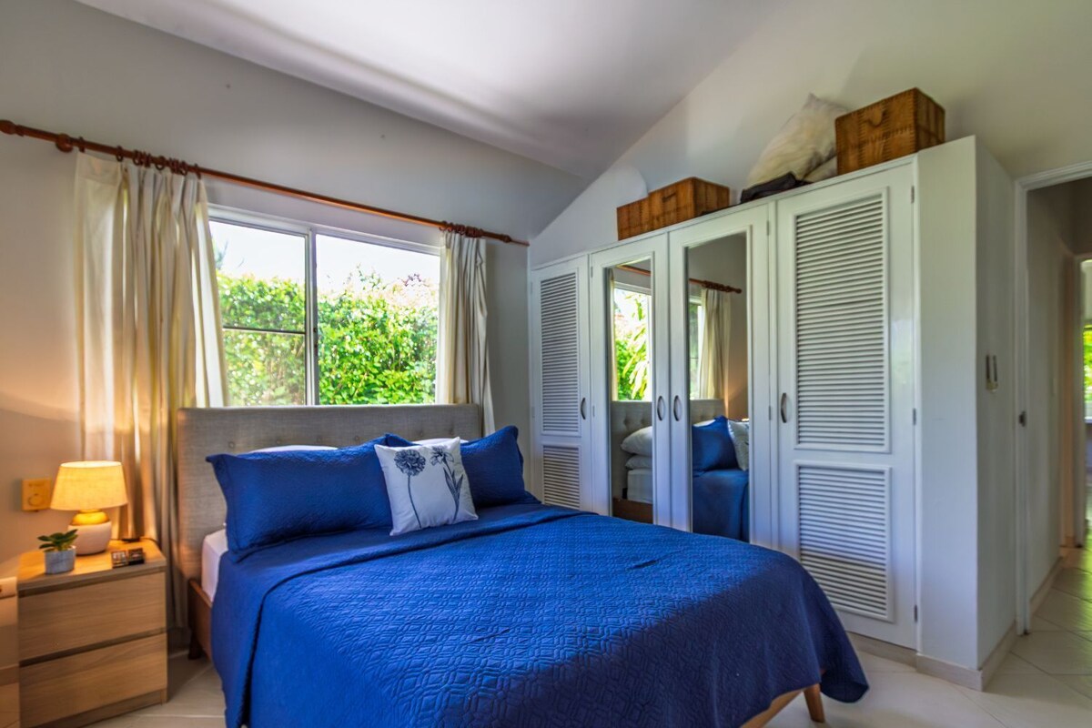 Um quarto com cama, mesa de cabeceira, guarda-roupa e janela com cortinas.
