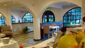 Uma área de refeições com mesas, frutas e janelas em arco.