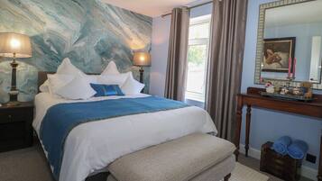 Um quarto com cama, abajures, cômoda, espelho e janela com cortinas.