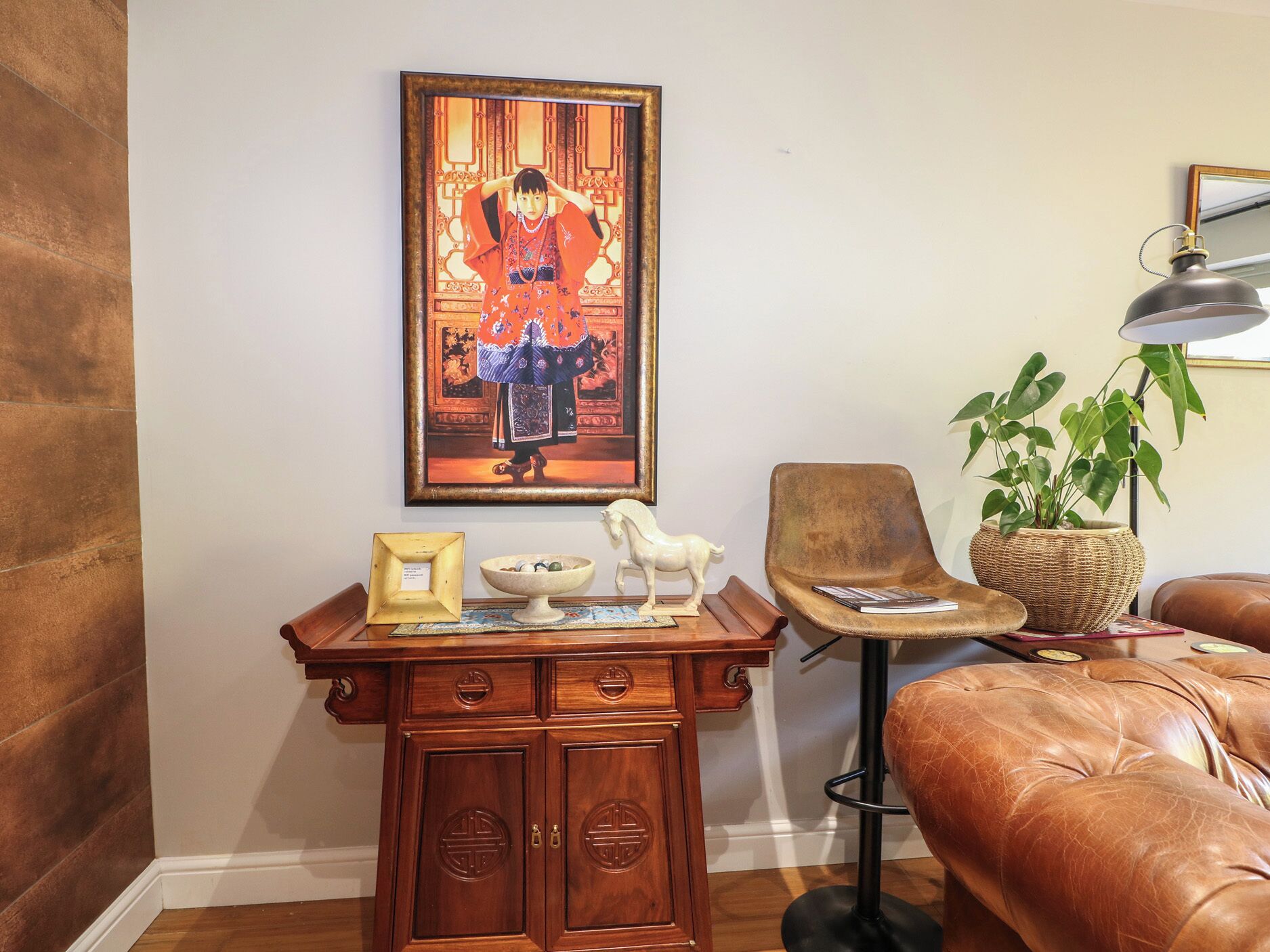Um quarto com um armário de madeira, um quadro emoldurado, uma cadeira, uma mesa e um abajur.