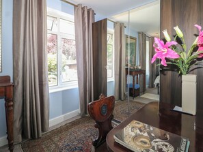 Quarto com um espelho grande, uma escrivaninha de madeira, uma cadeira, um tapete e uma janela com cortinas.