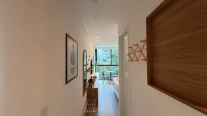 Corredor com quadros emoldurados, porta de madeira e vista para uma varanda com móveis de exterior.