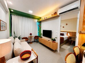 Quarto de hotel moderno com sofá, mesa de jantar, televisão e área de dormir separada.