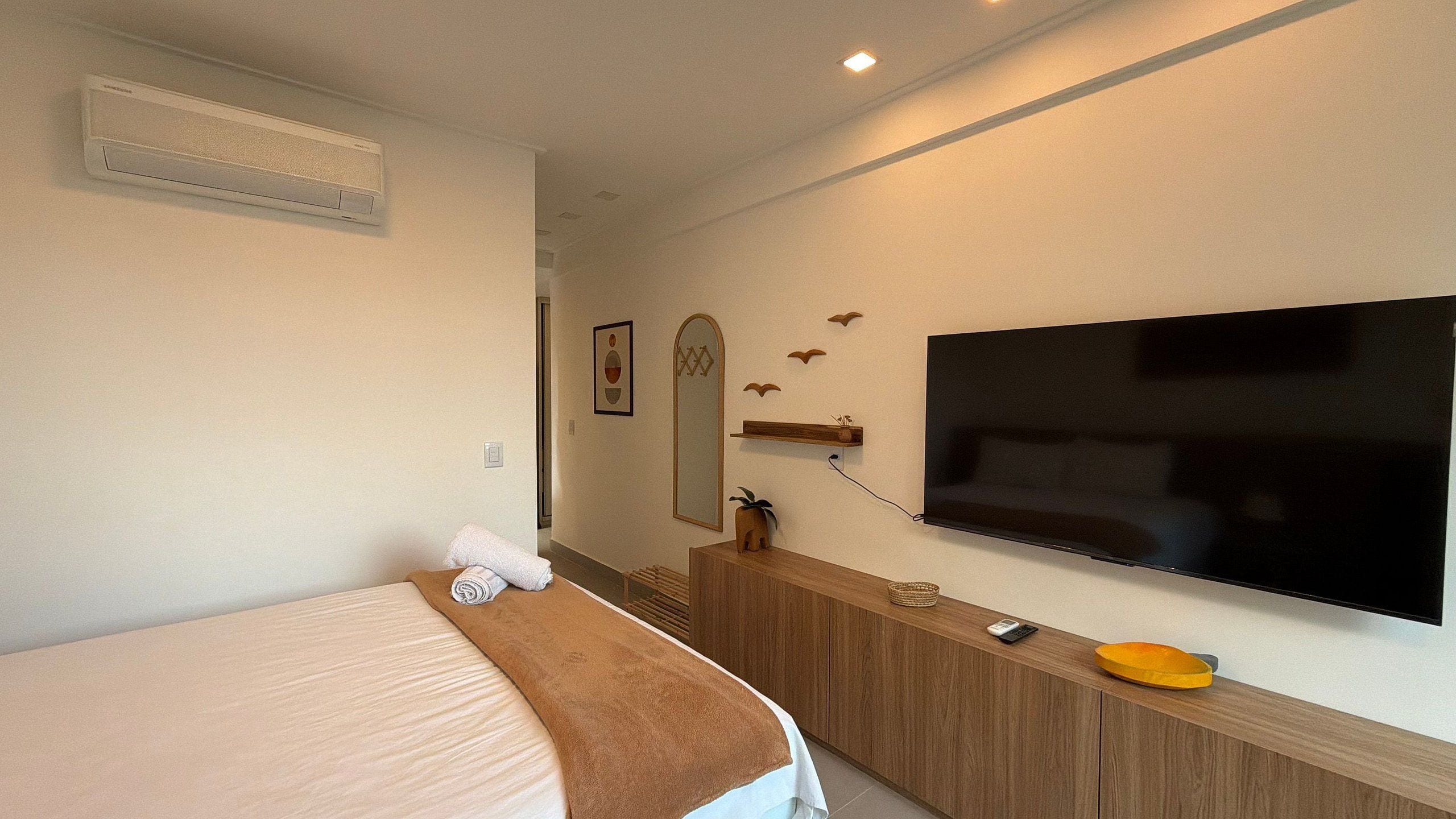 Quarto de hotel com uma cama, televisão de tela plana na parede, um armário de madeira e uma toalha sobre a cama.